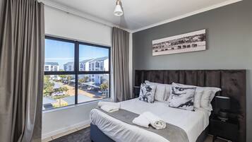 Quarto moderno com uma cama grande, vista de um complexo de edifícios e um quadro na parede.