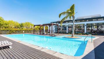 Uma piscina moderna ao ar livre com um deck de madeira, uma área de estar coberta e uma palmeira.