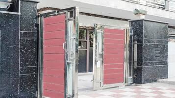 Entrada de edifício com piso xadrez, porta vermelha e câmera de segurança.