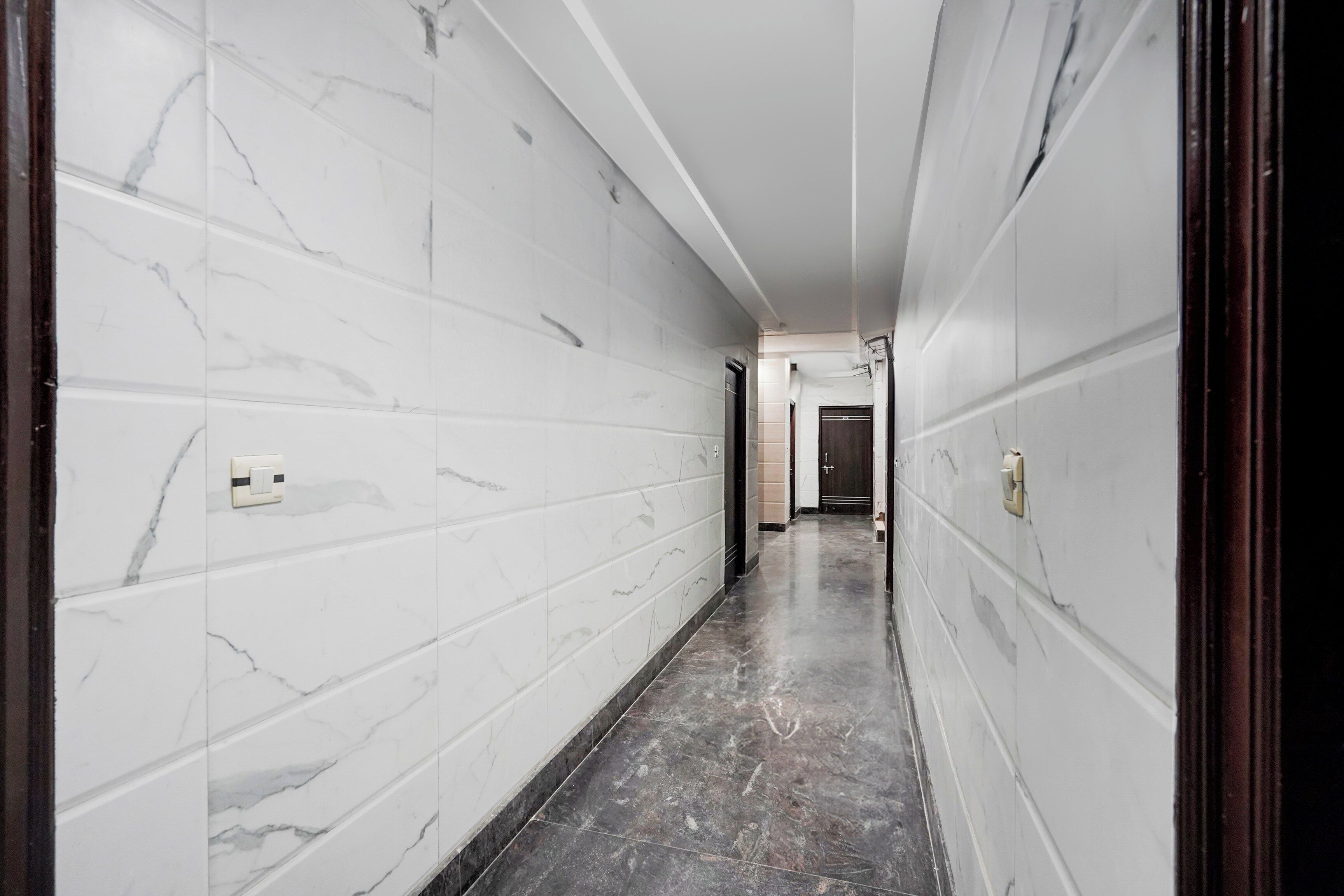 Um corredor com paredes de mármore e chão polido, que leva a uma porta no final.