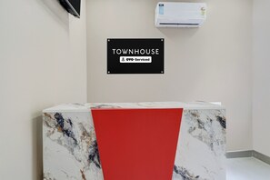 Uma receção com bancada de mármore e detalhes vermelhos, uma placa acima com a inscrição 'TOWNHOUSE OYO-Serviced', e um aparelho de ar condicionado fixado na parede.