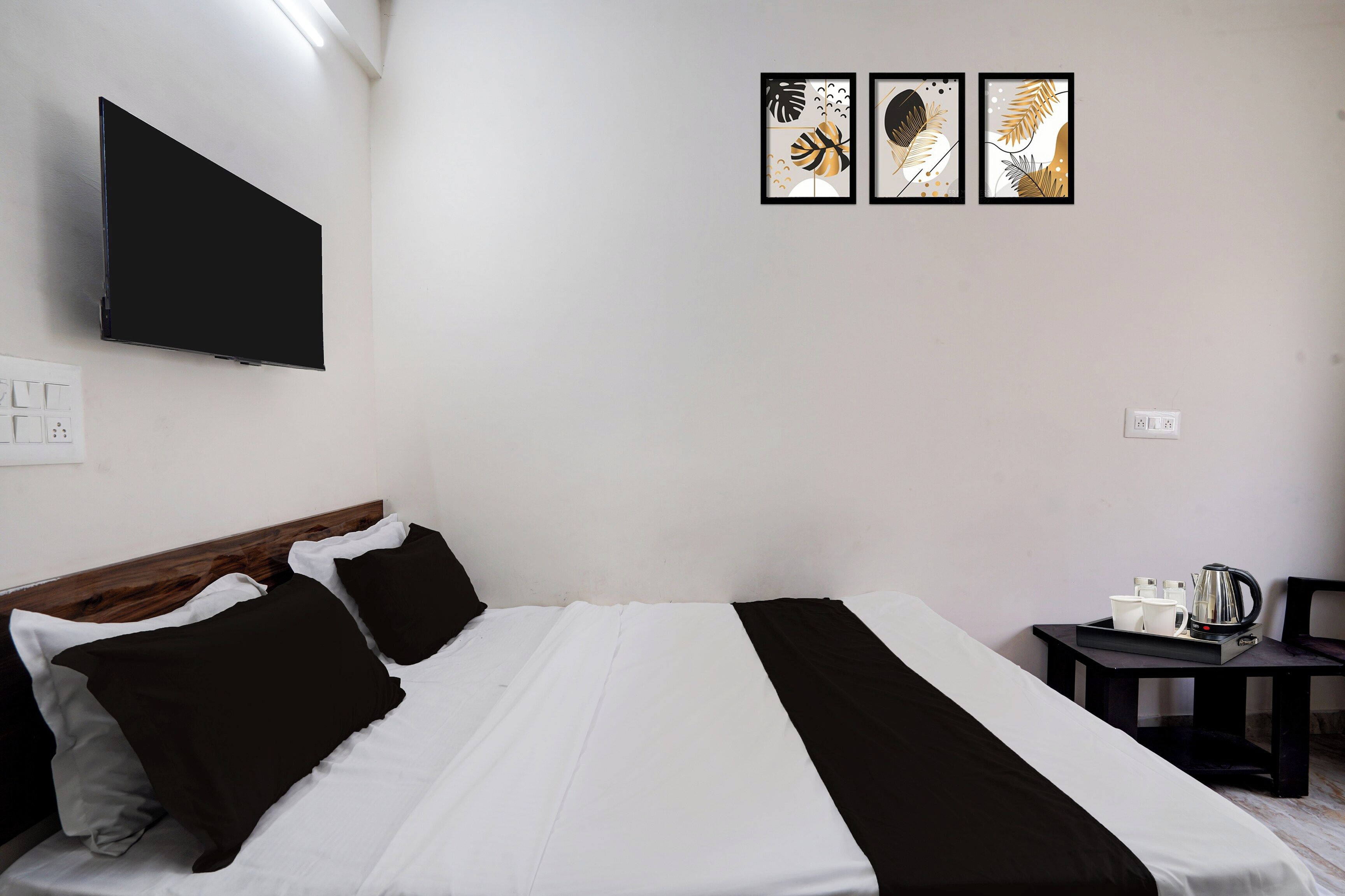 Quarto de hotel com uma cama, televisão de tela plana fixada na parede e três obras de arte emolduradas acima da cama.