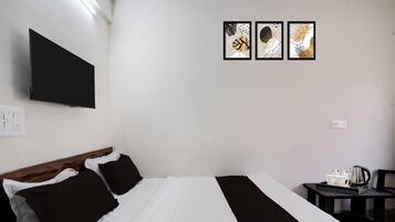 Quarto de hotel com uma cama, televisão de tela plana fixada na parede e três obras de arte emolduradas acima da cama.