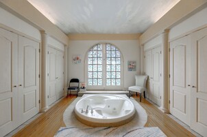 Um banheiro espaçoso com uma banheira separada, uma ampla janela em arco e piso revestido de azulejos brancos.