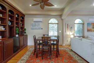 Uma sala de jantar com uma mesa e cadeiras de madeira, um tapete decorativo e uma estante com diversos objetos.