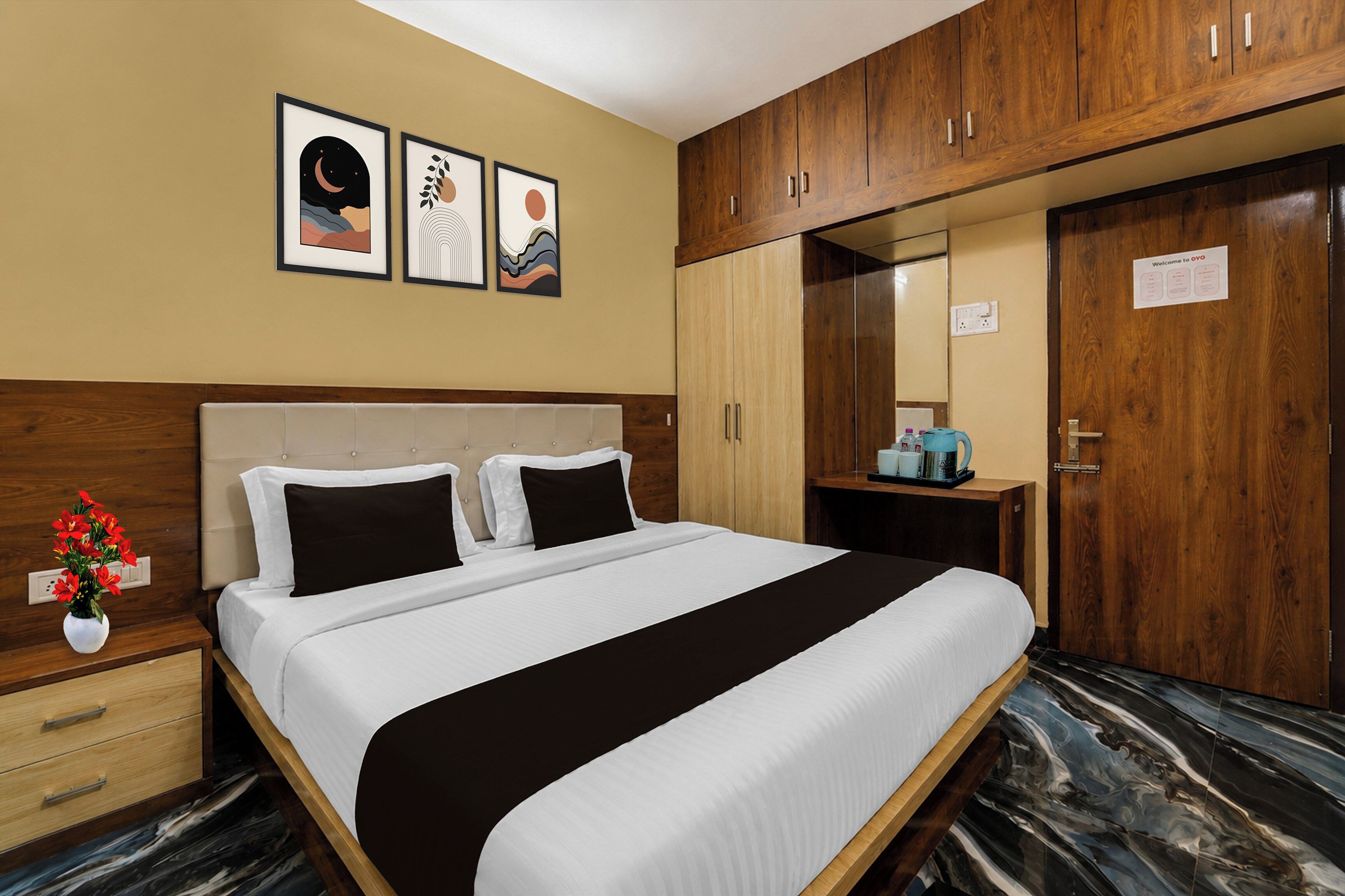 Quarto de hotel com cama, mesa de cabeceira com um vaso de flores, guarda-roupa e espelho.