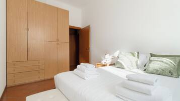 Quarto de hotel com um guarda-roupa espaçoso, cama bem arrumada com roupa de cama branca e mesa de cabeceira com abajur.