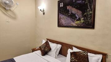 Quarto de hotel com cama, ventilador fixado na parede, luz noturna e almofada com estampa de leopardo.