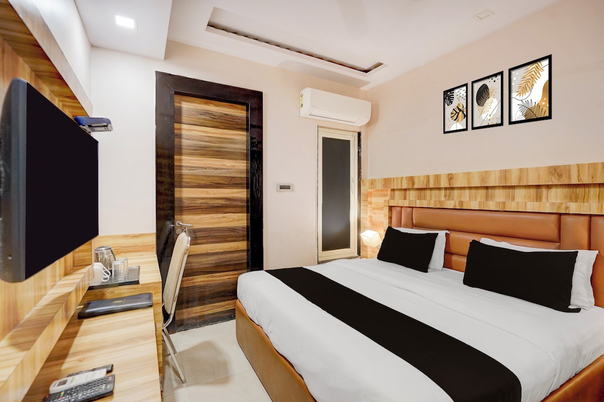 Quarto de hotel com cama, mesa de cabeceira, televisão e porta de madeira.