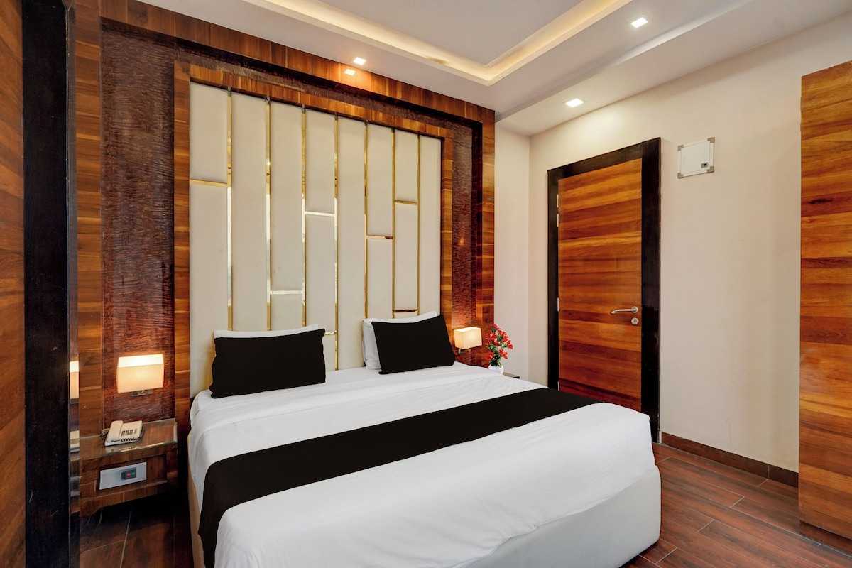 Quarto de hotel com uma cama grande, painéis de madeira, uma mesa de cabeceira com telefone e uma porta com puxador.