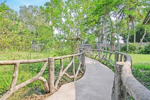 Uma trilha de madeira curva com grades, cercada por vegetação exuberante e árvores.