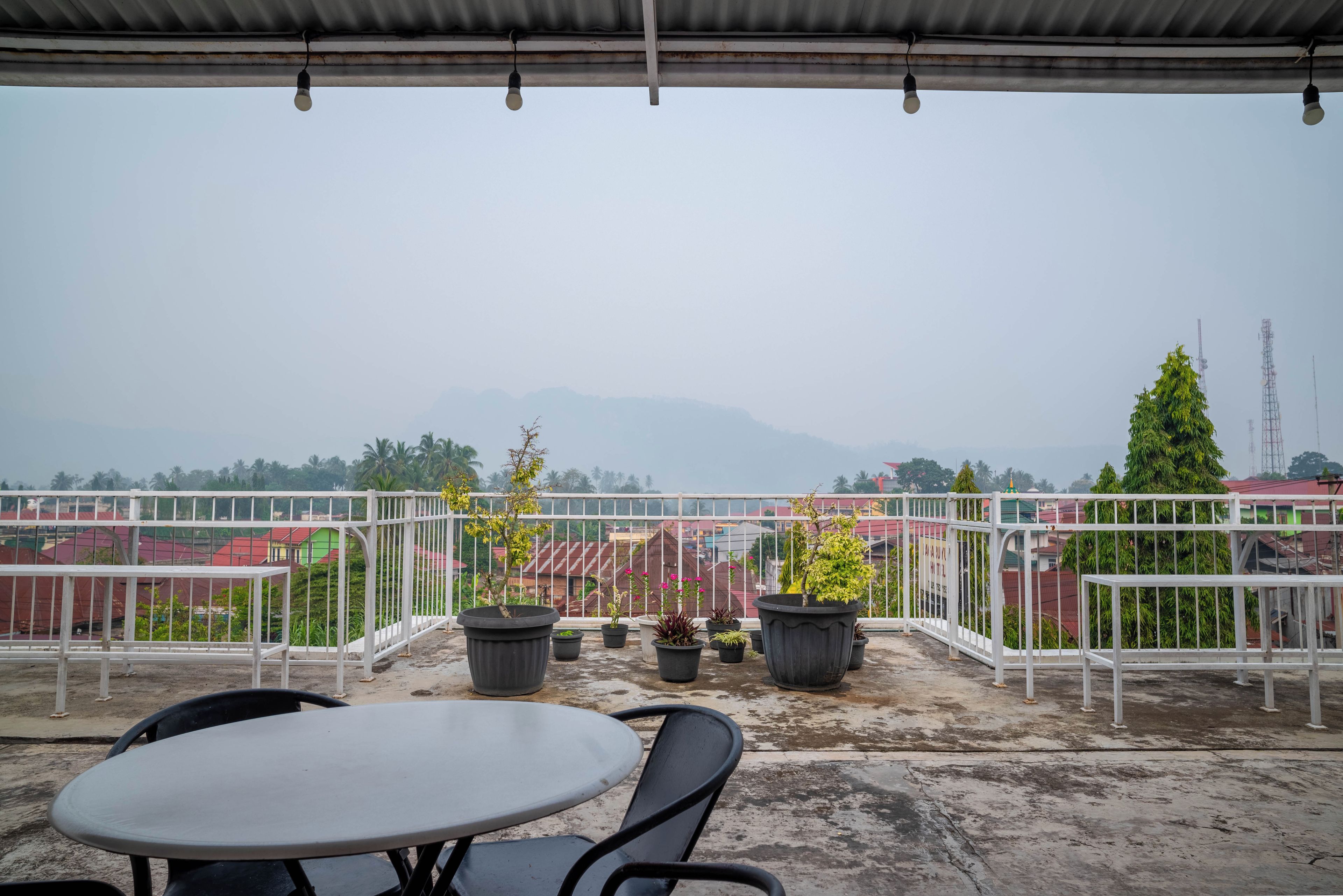 Terraço no telhado com mesa e cadeiras, plantas em vasos e vista de prédios e montanhas ao longe.