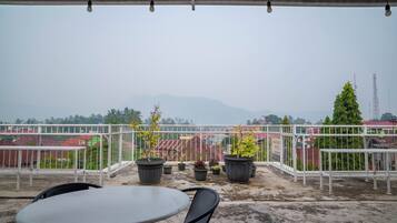 Terraço no telhado com mesa e cadeiras, plantas em vasos e vista de prédios e montanhas ao longe.
