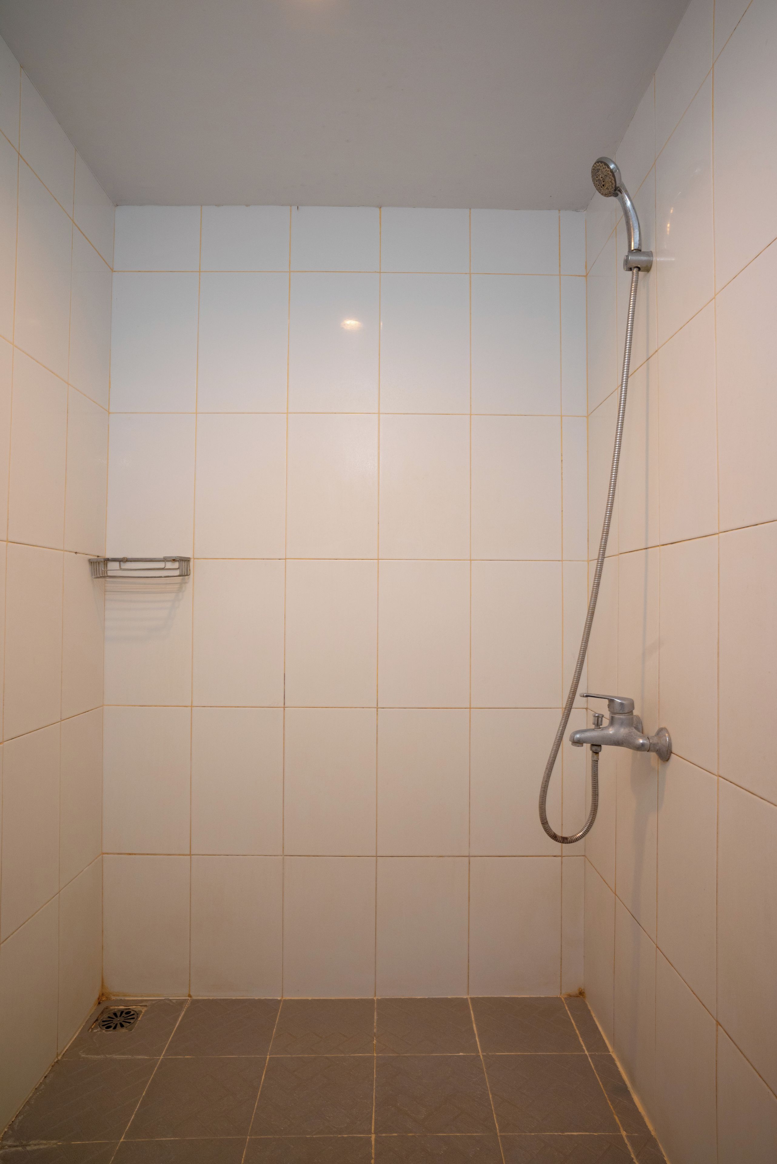 Um pequeno banheiro revestido com azulejos, com chuveiro manual e torneira fixa na parede.