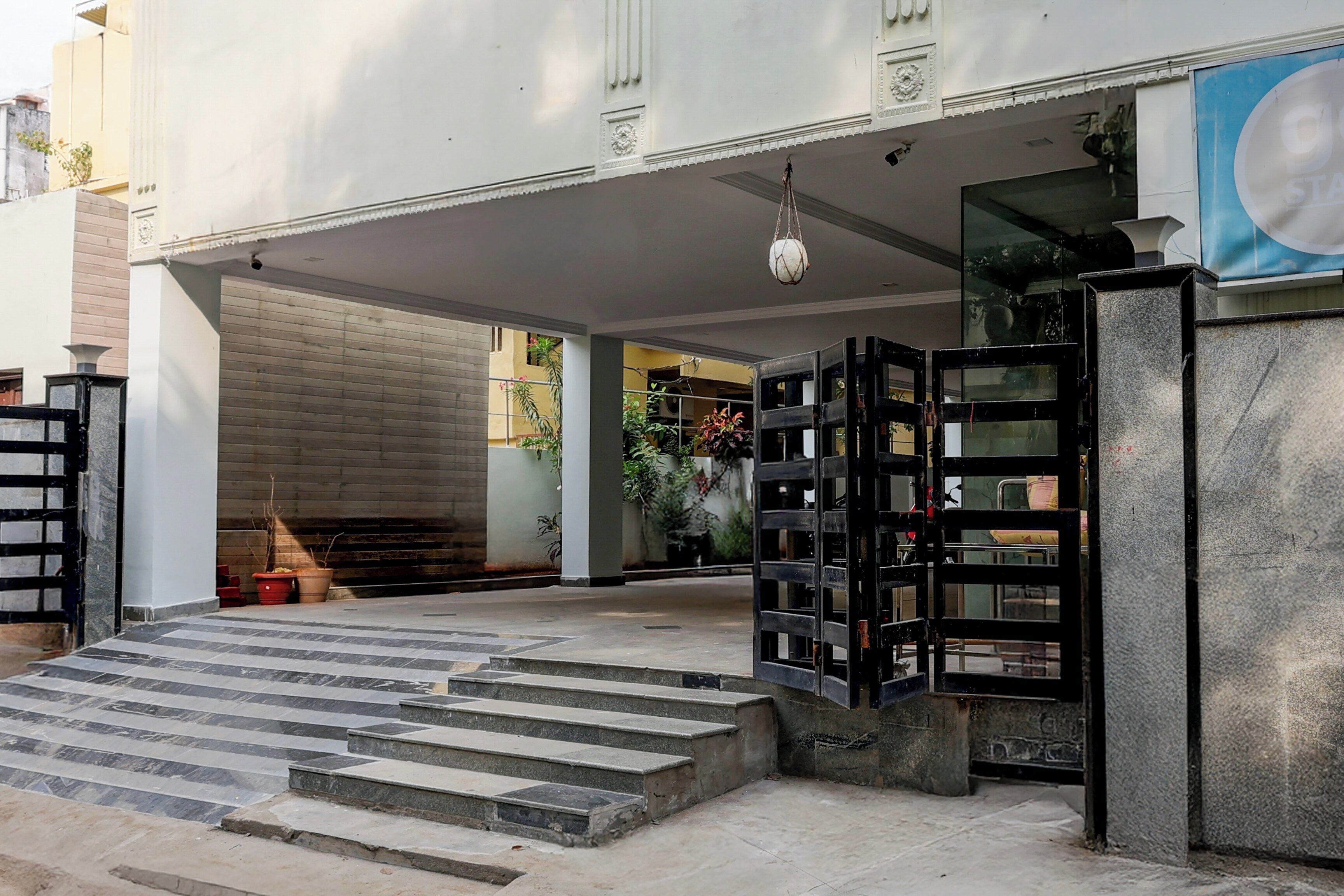 Entrada de um edifício com escadas que levam a uma área coberta, um amplo espaço aberto com ventilador de teto e um portão de metal preto.