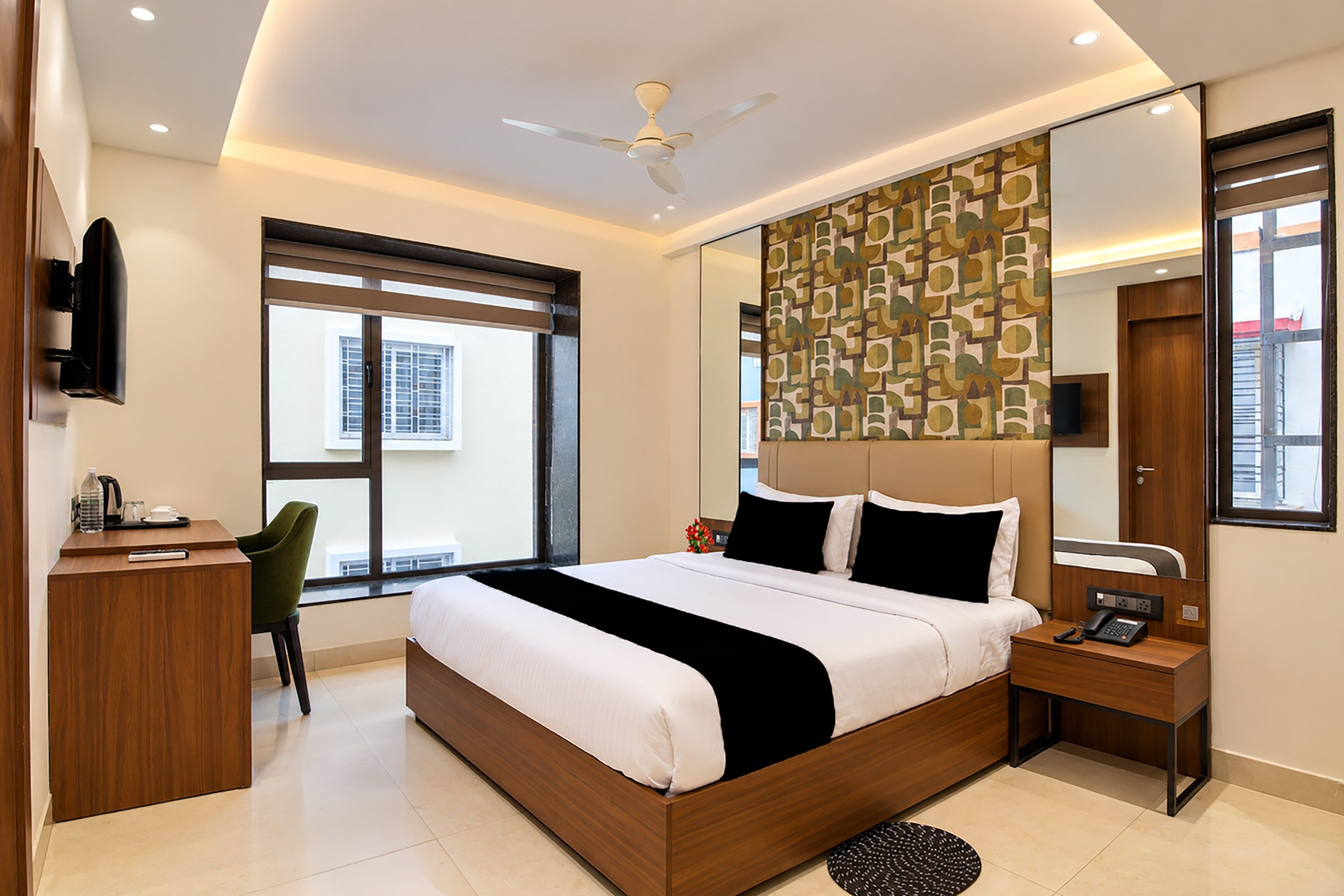 Quarto de hotel moderno com uma cama grande, escrivaninha, cadeira, espelho e ventoinha no teto.