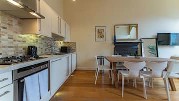 Uma cozinha moderna com armários brancos, fogão de aço inoxidável e mesa de jantar de madeira com cadeiras brancas.