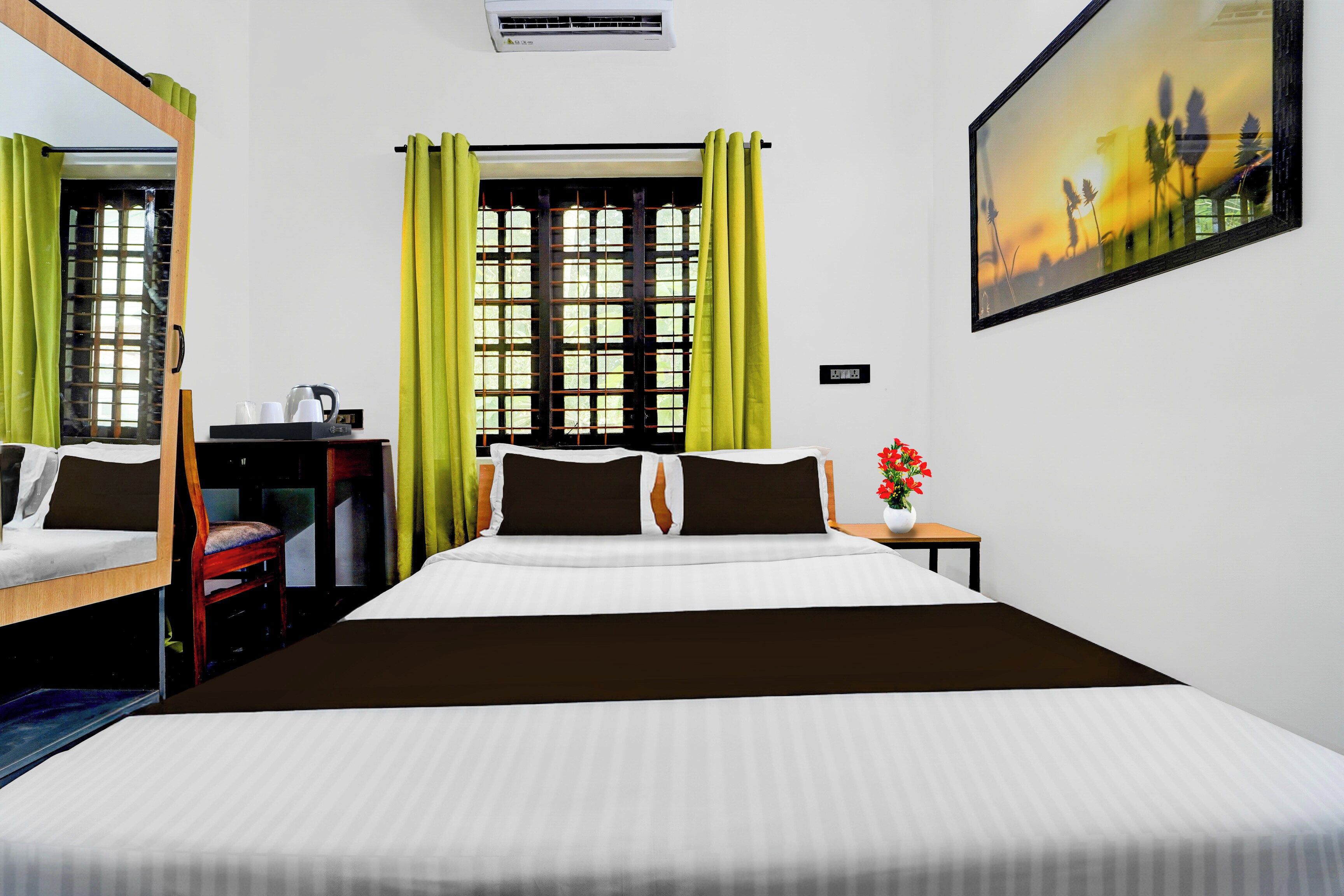 Quarto de hotel com uma cama, uma escrivaninha com cadeira, um espelho, uma janela com cortinas e um quadro na parede.
