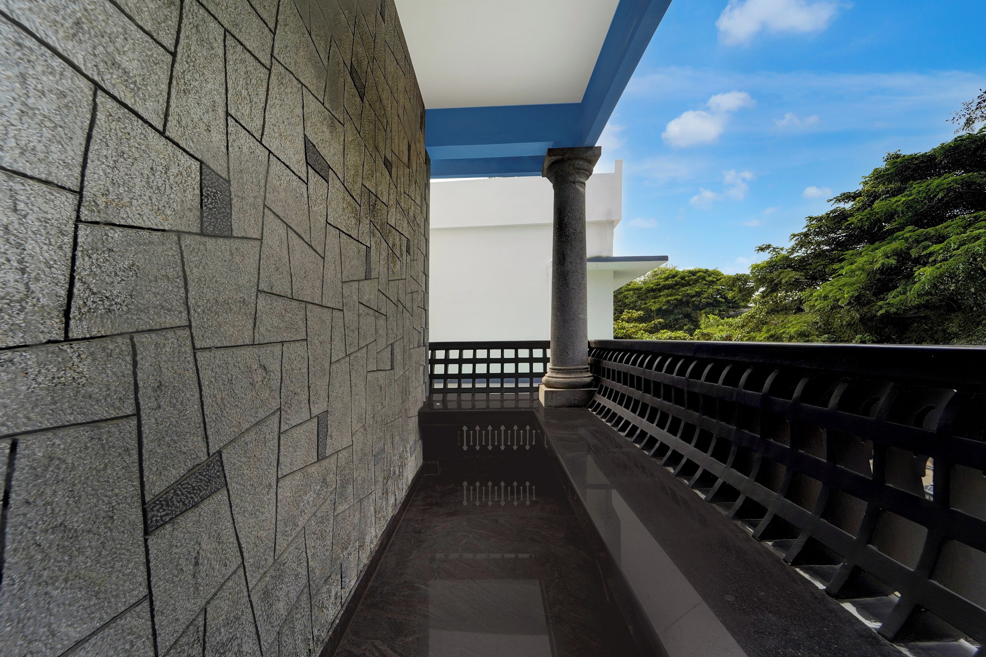 Corredor com paredes de pedra, corrimão preto e céu claro.