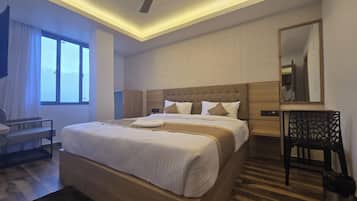 Quarto de hotel com cama, escrivaninha, cadeira, ventoinha no teto e uma janela grande.