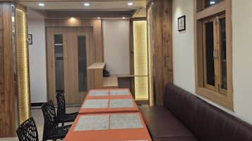 Uma sala de conferências com uma mesa comprida, cadeiras pretas, um sofá castanho, detalhes em madeira e iluminação embutida no teto.