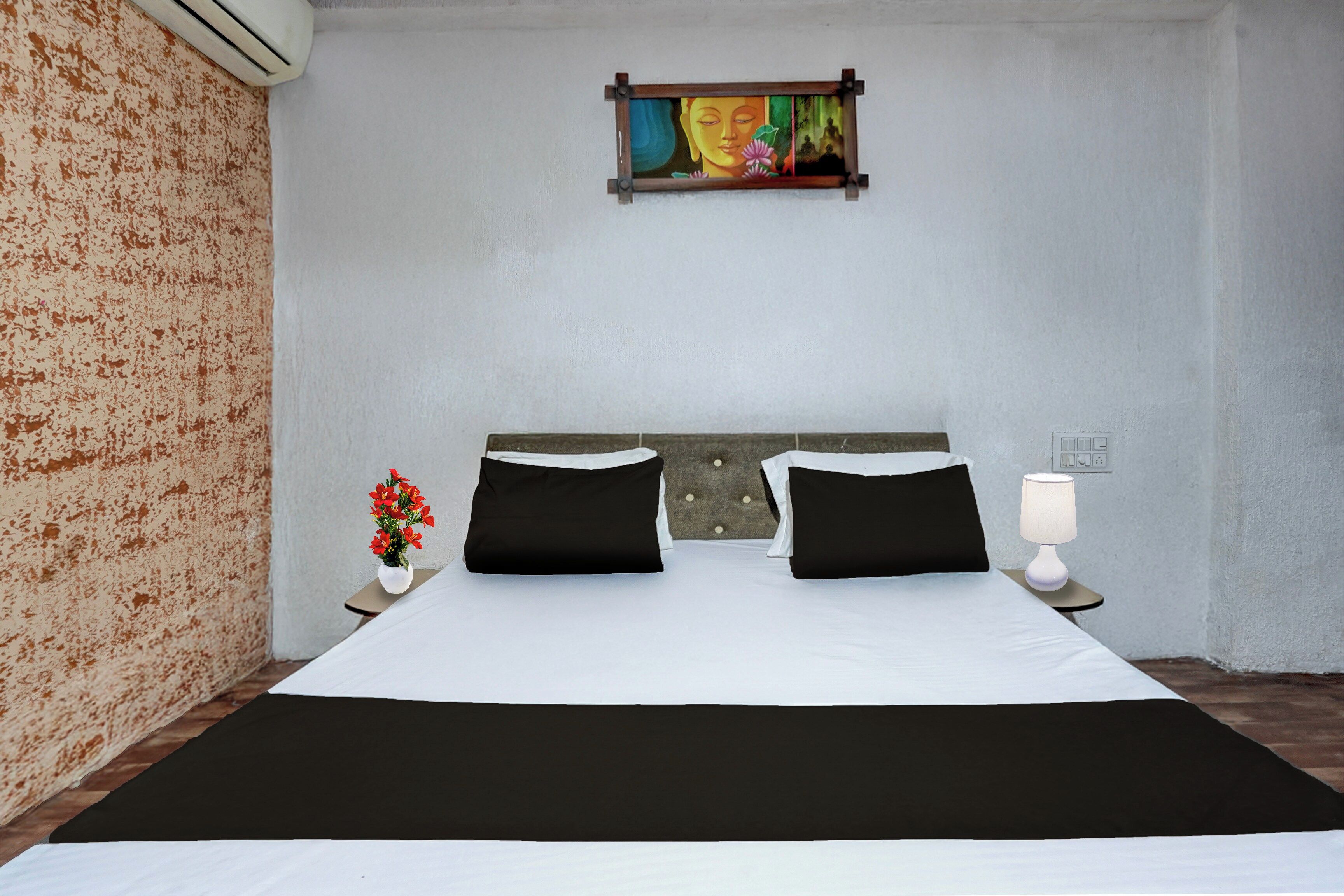 Quarto de hotel com cama, mesa de cabeceira, abajur e um quadro na parede.