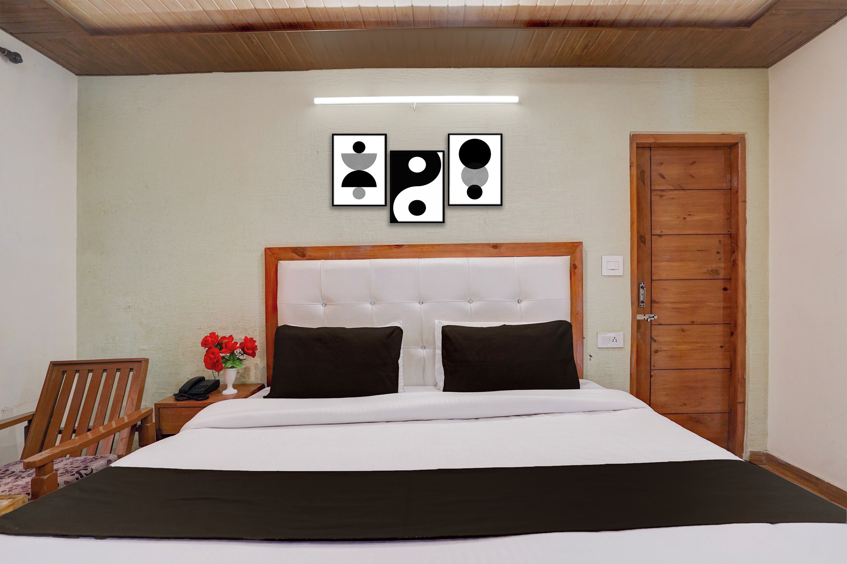 Quarto com cama, mesa de cabeceira, cadeira de madeira, porta de madeira e três quadros na parede.