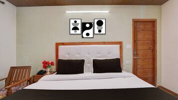 Quarto com cama, mesa de cabeceira, cadeira de madeira, porta de madeira e três quadros na parede.