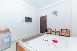 Quarto de hotel com cama, duas cadeiras, uma mesa pequena, televisão e frigorífico.