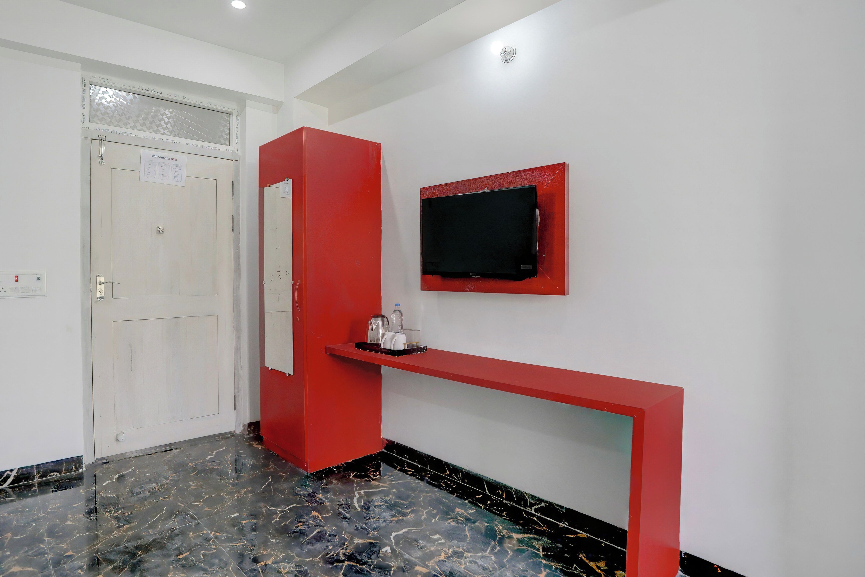 Uma área de recepção com porta branca, console vermelho e televisão na parede.