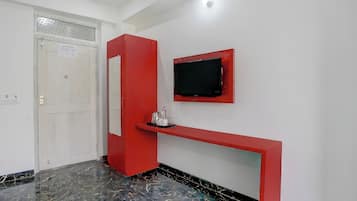 Uma área de recepção com porta branca, console vermelho e televisão na parede.