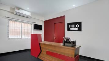 Balcão de recepção de hotel com esquema de cores vermelho e preto, uma televisão de tela plana na parede e uma placa indicando que o hotel é para uso corporativo.