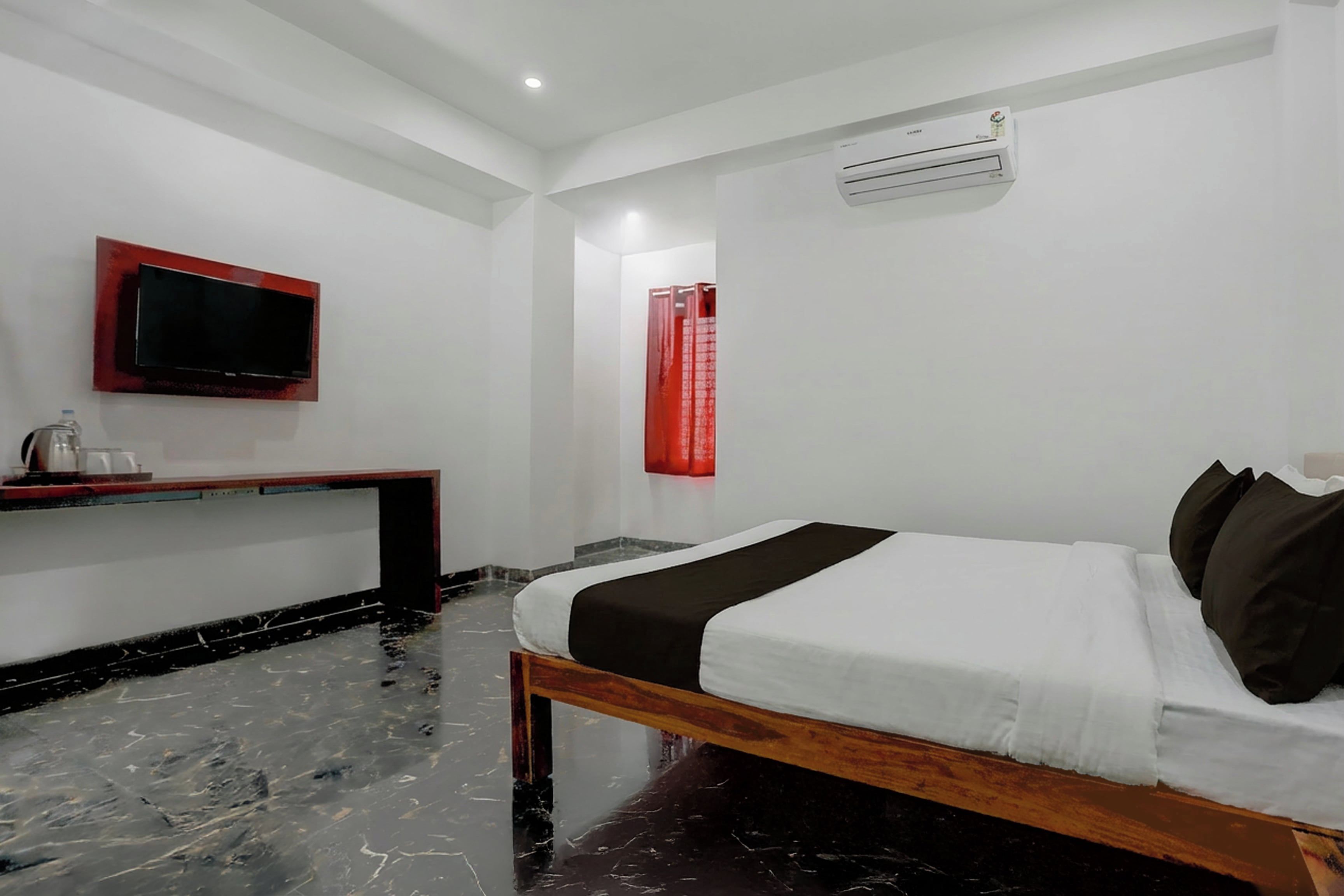 Quarto de hotel com cama, escrivaninha, televisão e ar condicionado.