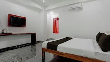 Quarto de hotel com cama, escrivaninha, televisão e ar condicionado.