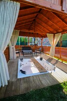 Um deck de madeira com hidromassagem, área de estar externa e espaço coberto com cortinas.