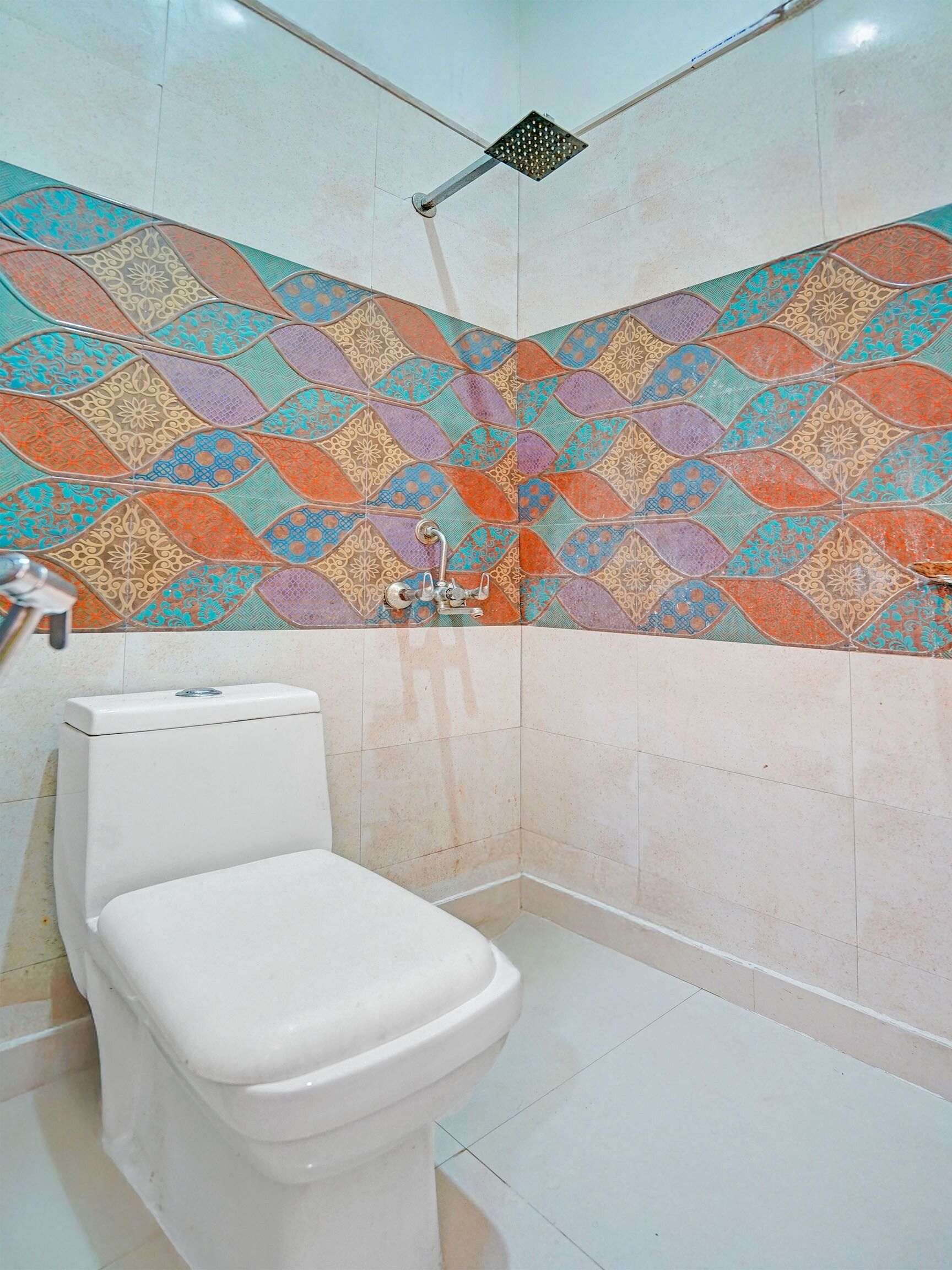 Casa de banho com sanita, chuveiro e parede com padrão de azulejos geométricos.