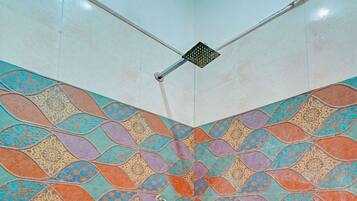 Casa de banho com sanita, chuveiro e parede com padrão de azulejos geométricos.