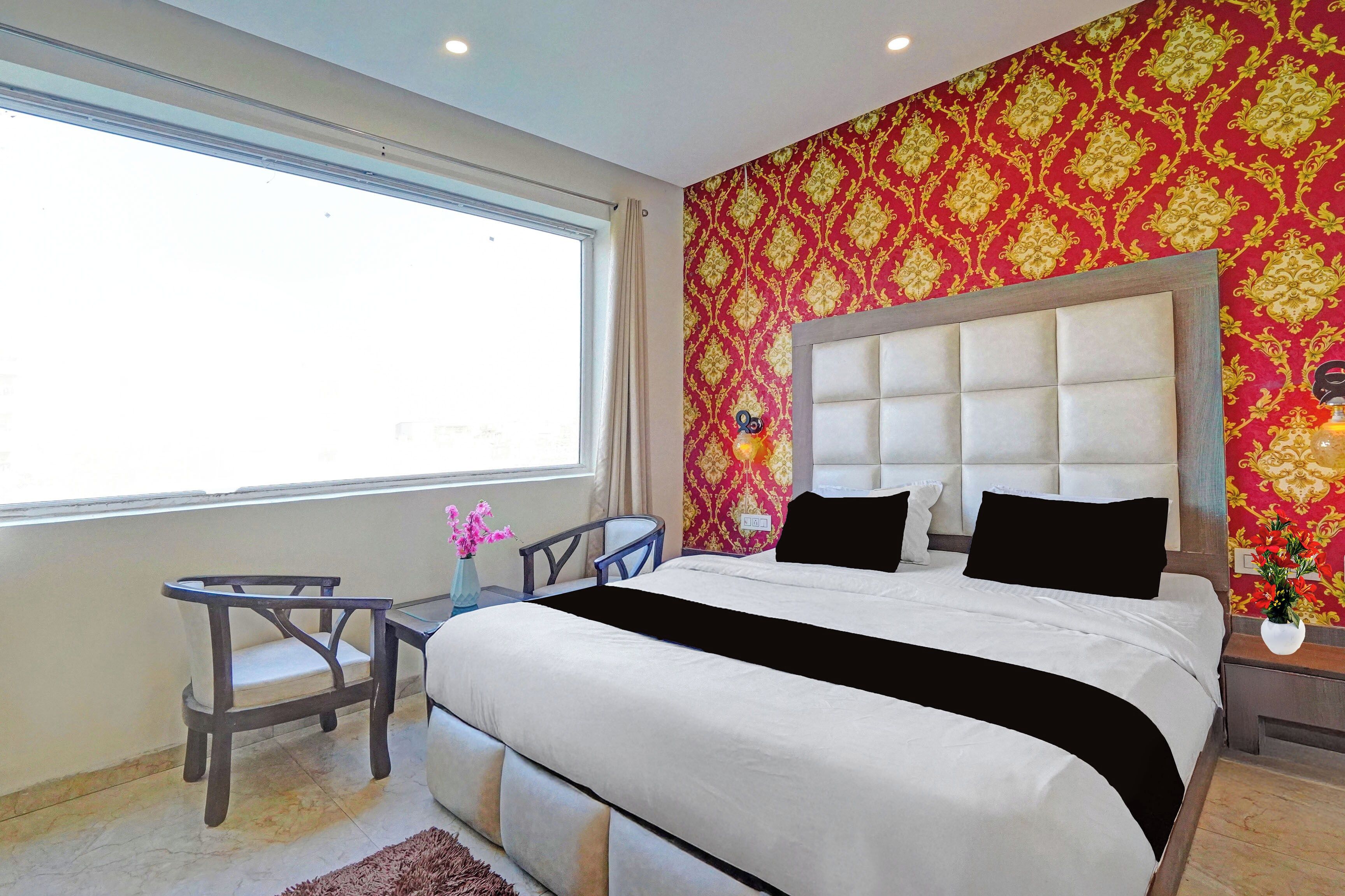 Quarto com cama grande, janela, cadeira e parede com papel de parede estampado.