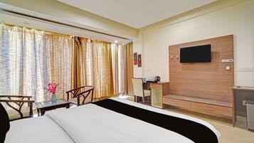 Quarto de hotel com cama, escrivaninha, cadeira, televisão na parede e cortinas.