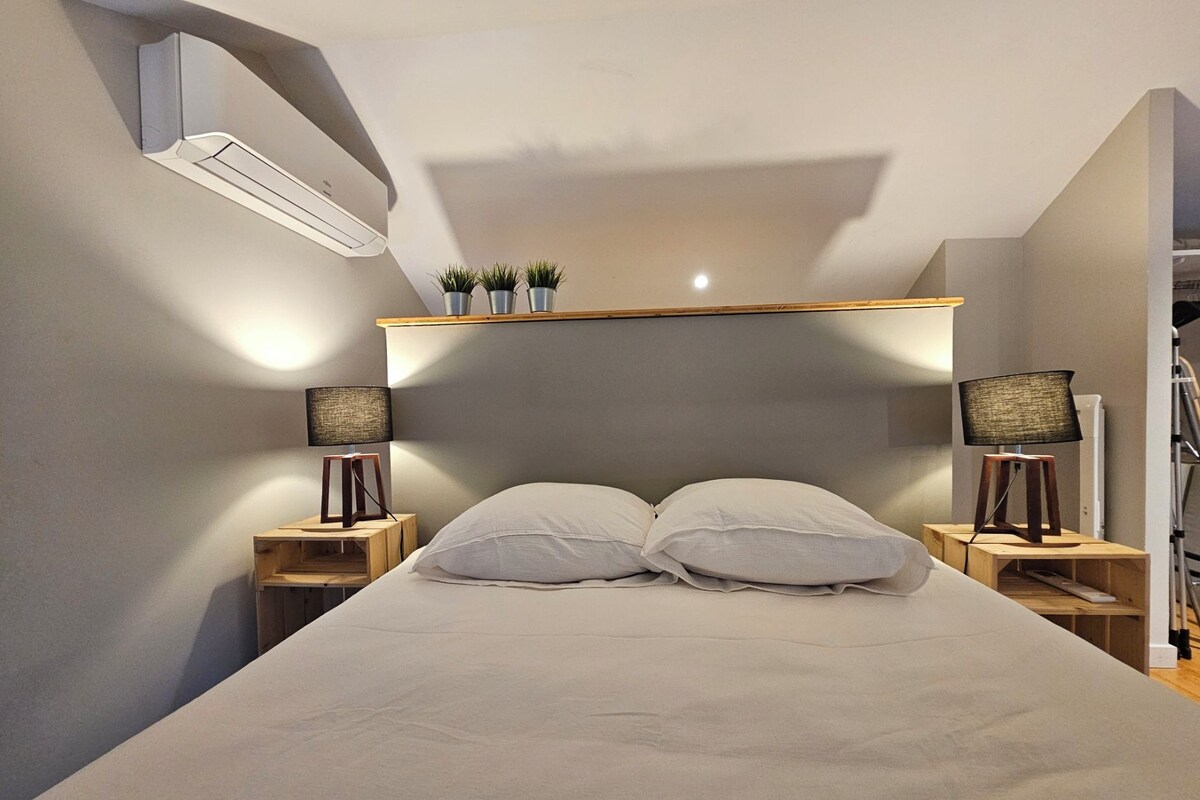 Quarto com cama, duas mesas de cabeceira com luminárias, uma estante com plantas e uma luminária no teto.