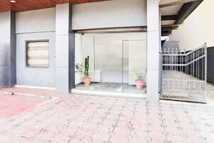 Entrada de um edifício com porta de vidro, plantas em vasos e portão de metal.