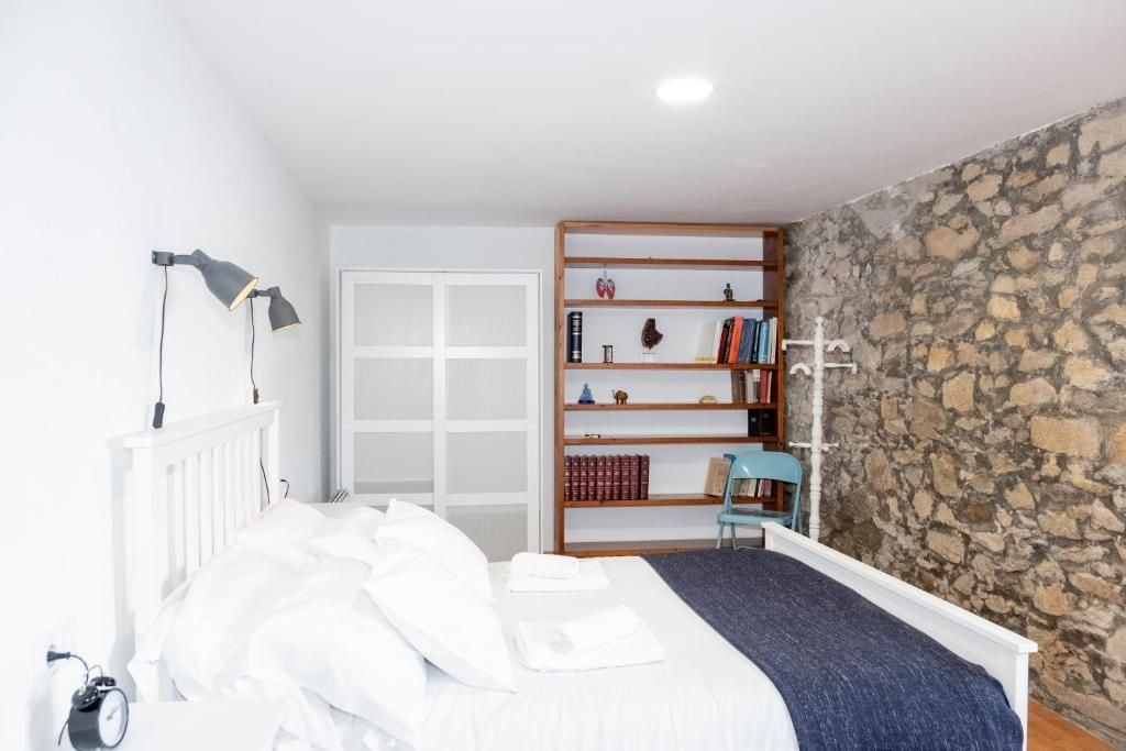 Quarto com cama, estante, escrivaninha e parede de pedra.