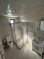 Casa de banho com sanita, cabine de duche envidraçada e lavatório com espelho em cima.