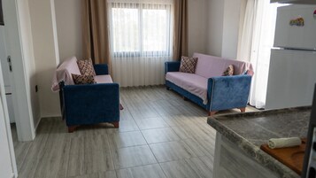 Um espaço habitável compacto com dois sofás, cozinha e janela com cortinas.