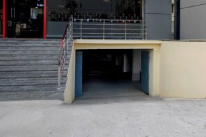 Escadaria de acesso a uma entrada de prédio, com corrimão de metal e plataforma de concreto.