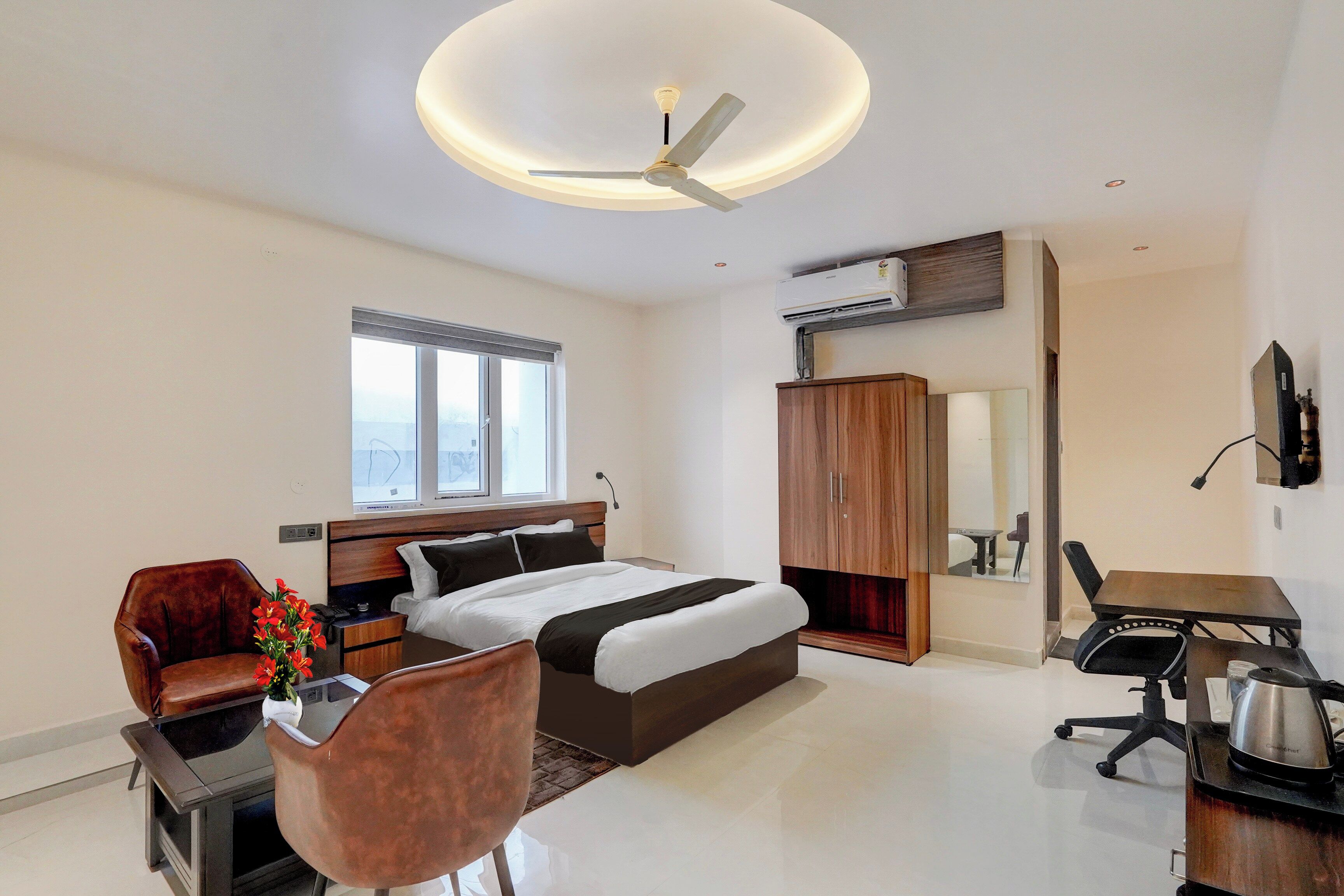 Quarto de hotel com cama, escrivaninha, cadeira, guarda-roupa e ventoinha no teto.