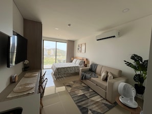Quarto de hotel moderno com cama, sofá, televisão e varanda com vista para edifícios.