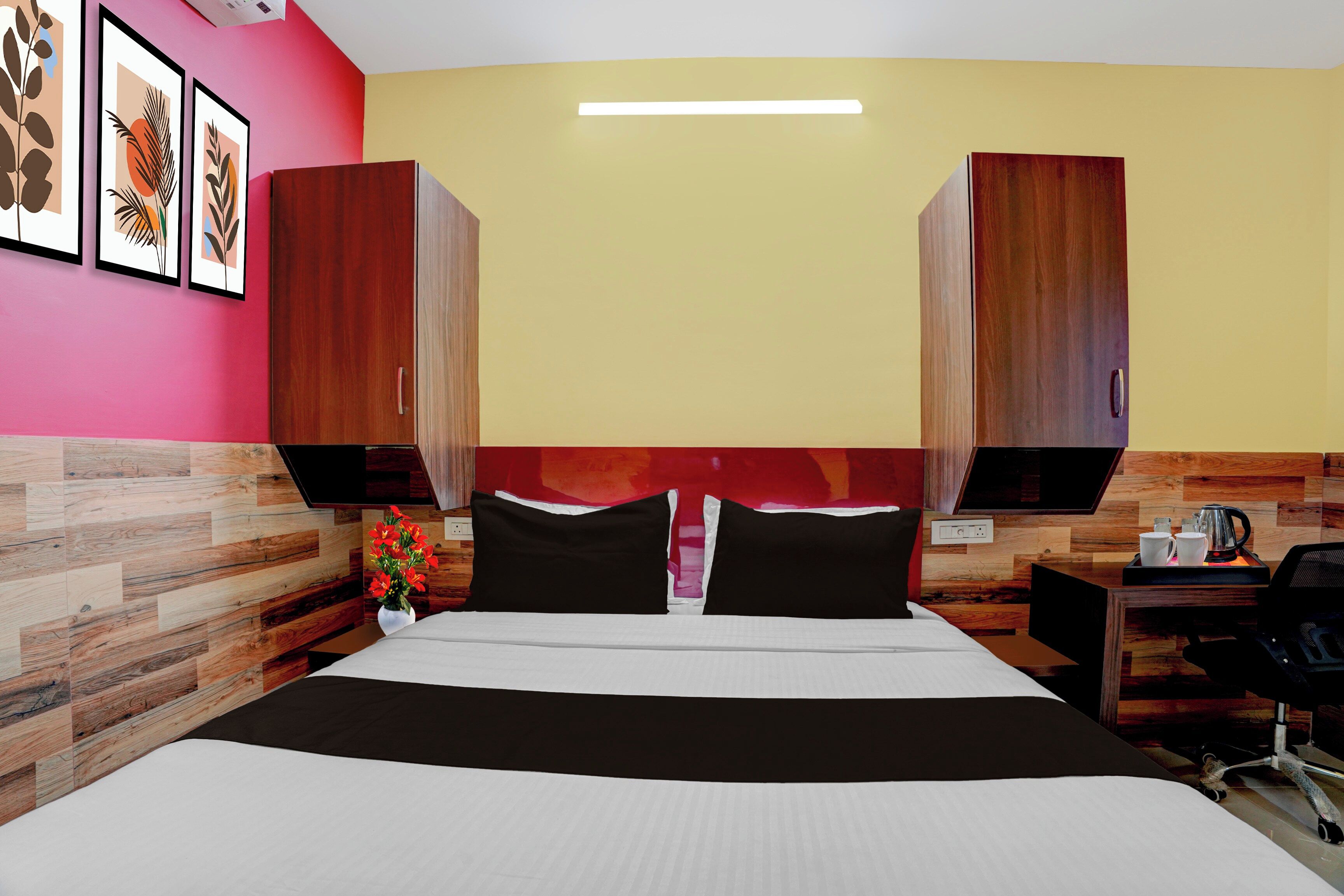 Quarto de hotel com cama, escrivaninha com cafeteira e parede decorada com obras de arte.