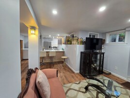 Uma sala de estar moderna com uma mesa de centro de vidro, um sofá com almofadas e uma televisão sobre um móvel.