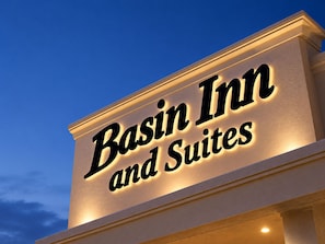 Placa indicativa do 'Basin Inn and Suites' com letras iluminadas contra um céu crepuscular.